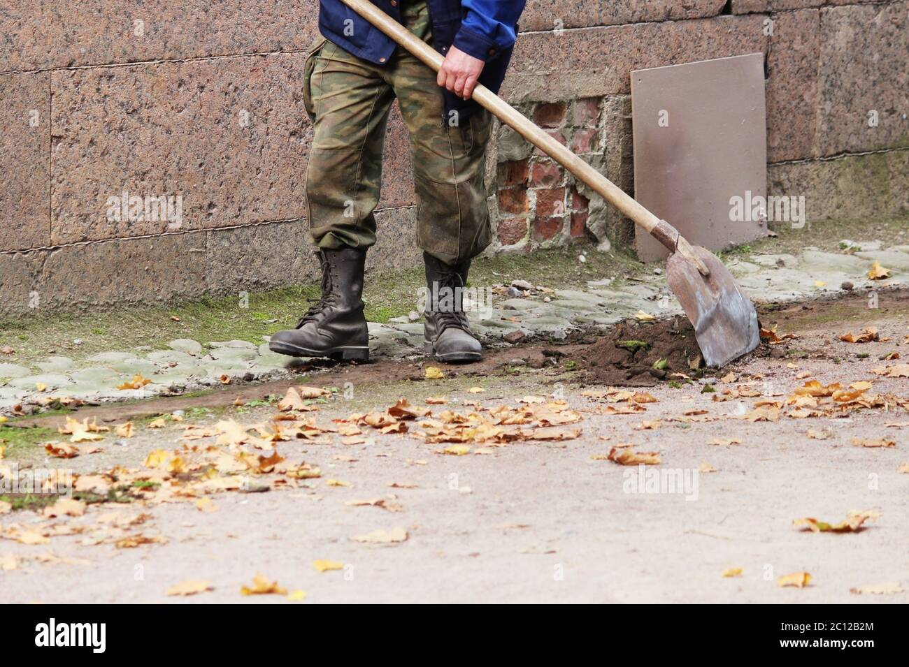 working man cleans a ditch with shovel of soil and sand near the palace ...