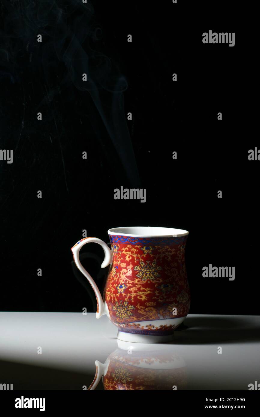 A red tea cup with designs on it placed on a white reflective table and ...