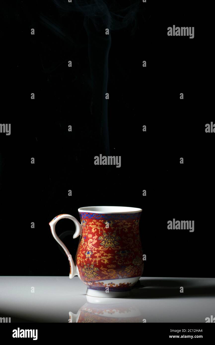 A red tea cup with designs on it placed on a white reflective table and ...