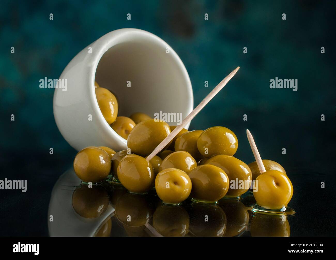 Green olives in a white porcelain cup and on a reflective surface with ...