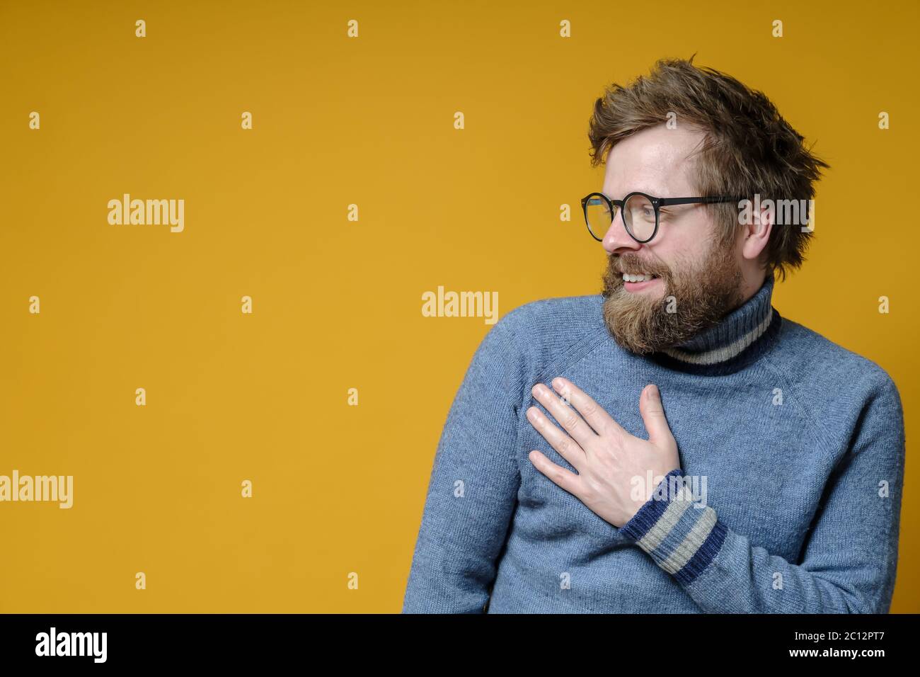 Cute modest man holds his hand on his chest and smiles good-naturedly ...