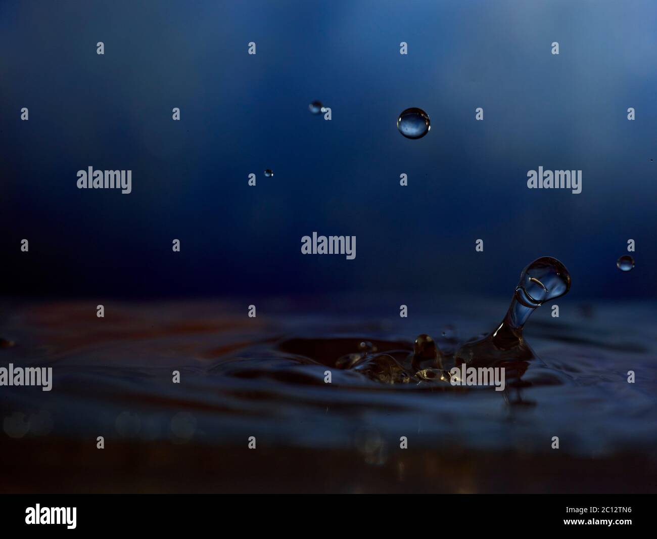 Water droplets falling on and bouncing off a pool of water, leaving ...