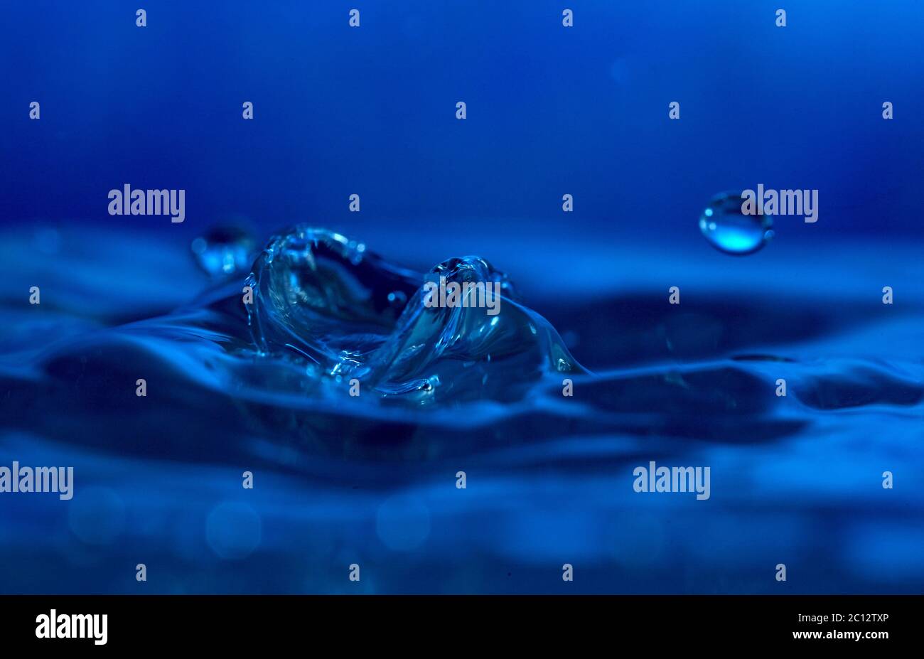 Water droplets falling on and bouncing off a pool of water, leaving ...