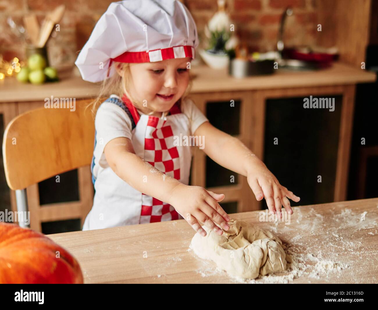 Little girl in cooking chef clothes enjoys kneading the dough. Girls at ...