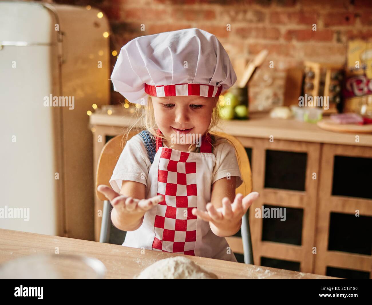 Little girl in cooking chef clothes enjoys kneading the dough. Girls at ...