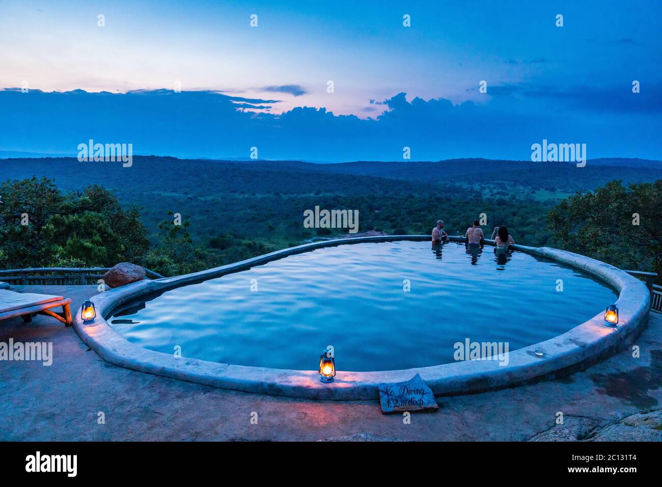 Three people relax at dusk in the swimming pool overlooking Lake Mburo ...