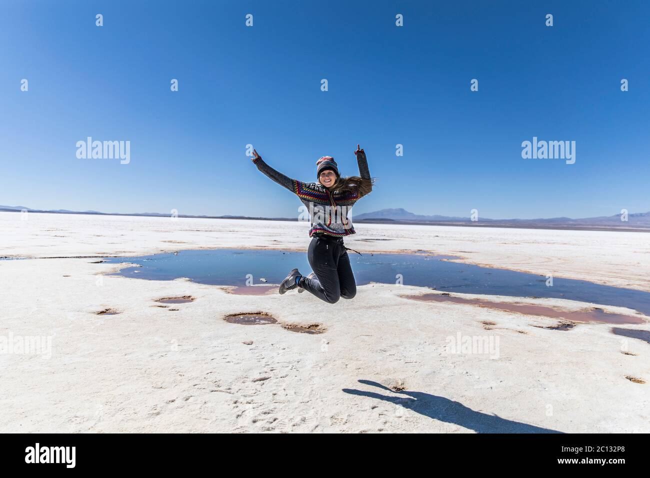 beautiful woman jumping in salt flats with blue sky in the background ...