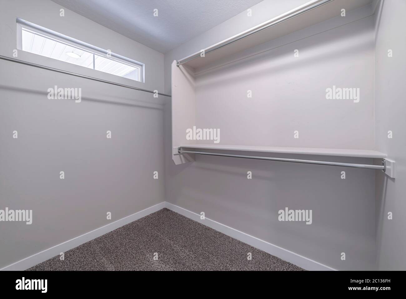 Empty walk in closet interior with small window carpet floor and white ...