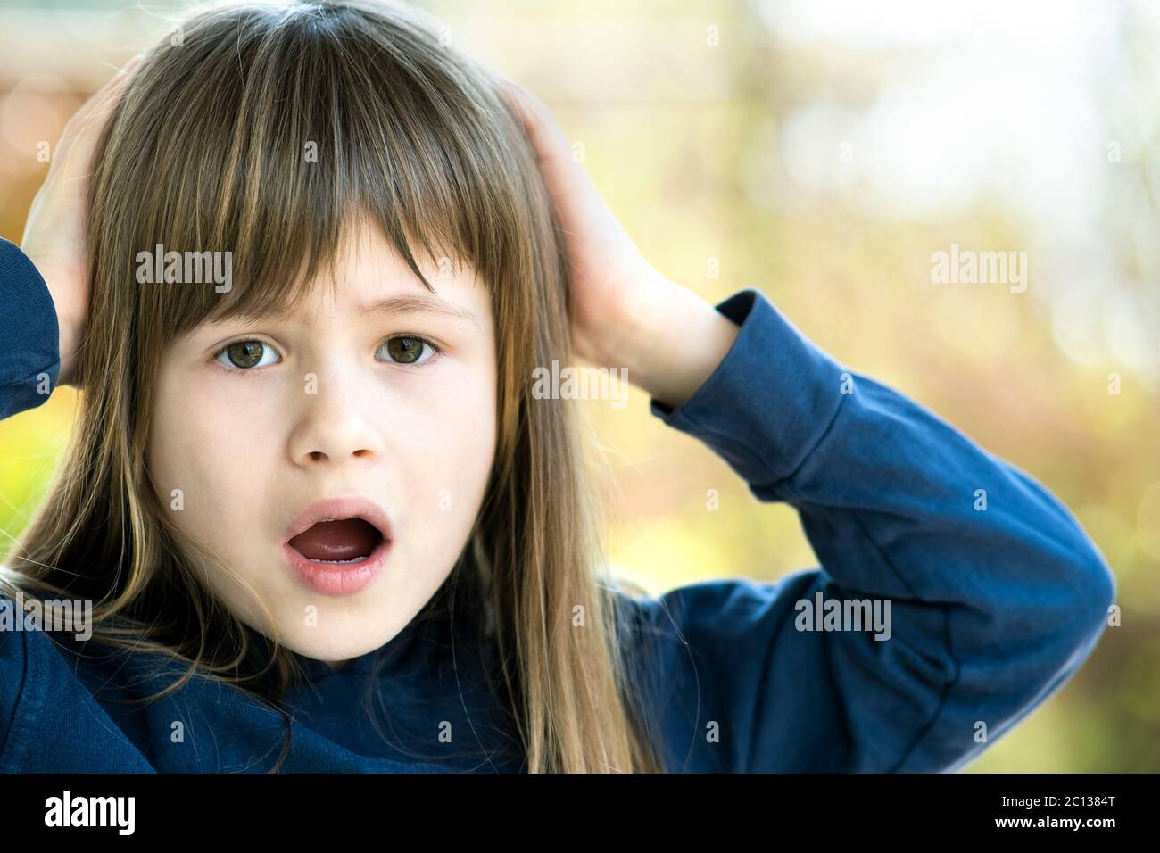 Portrait of surprised child girl holding hands to her head outdoors in ...