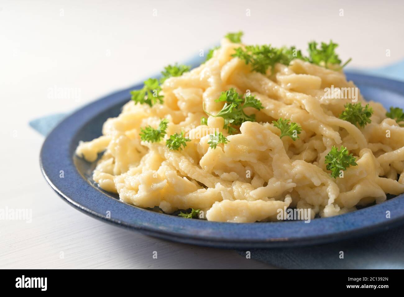 Homemade spaetzle with parsley garnish on a blue plate and a white ...