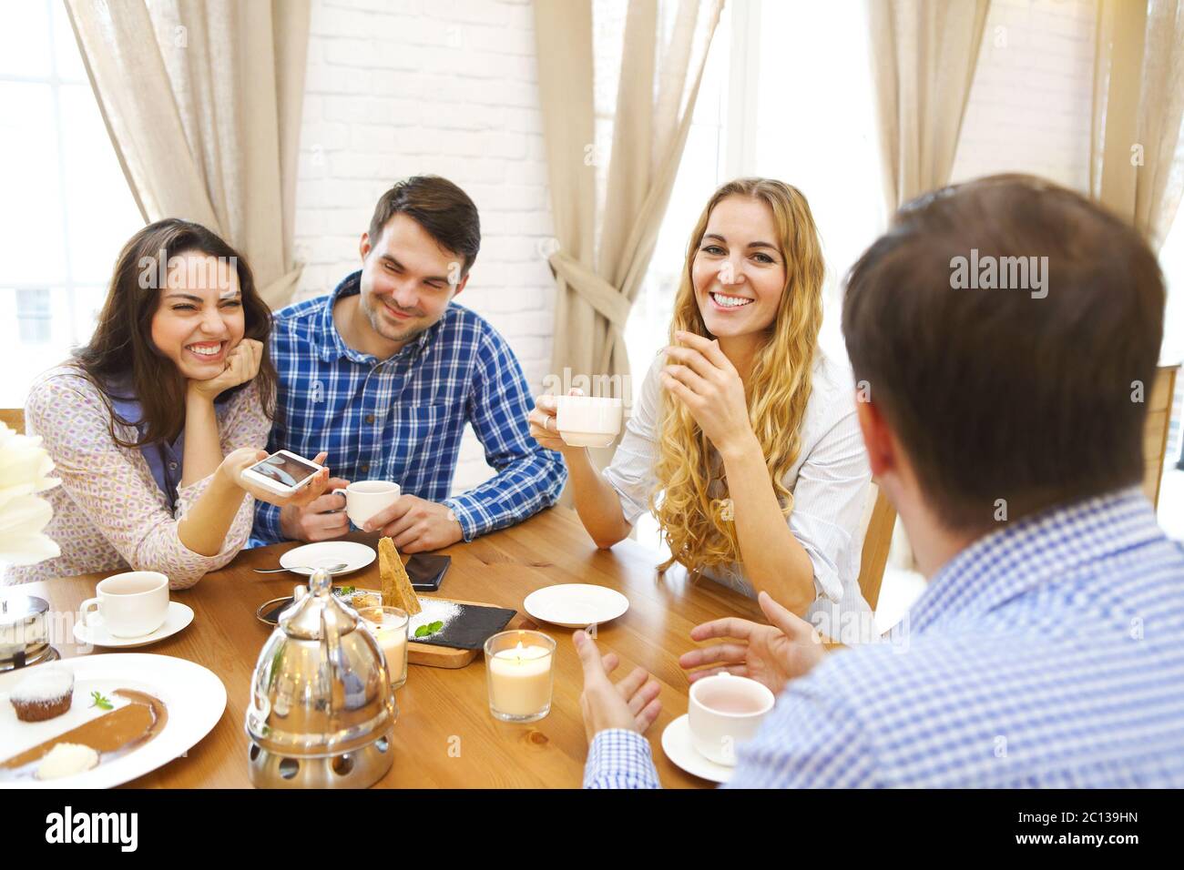 Group of four happy friends meeting and talking and eating desserts ...