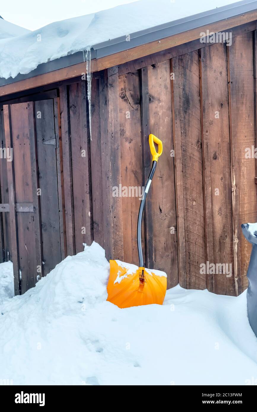 Yelllow snow shovel against snowed in ground and brown wooden wall of ...
