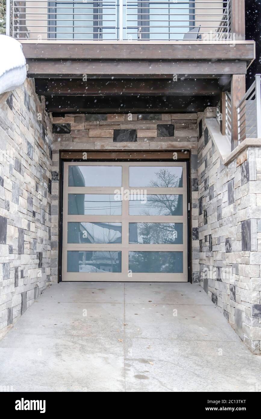 Snow falling down on home with glass panel garage door and stone ...