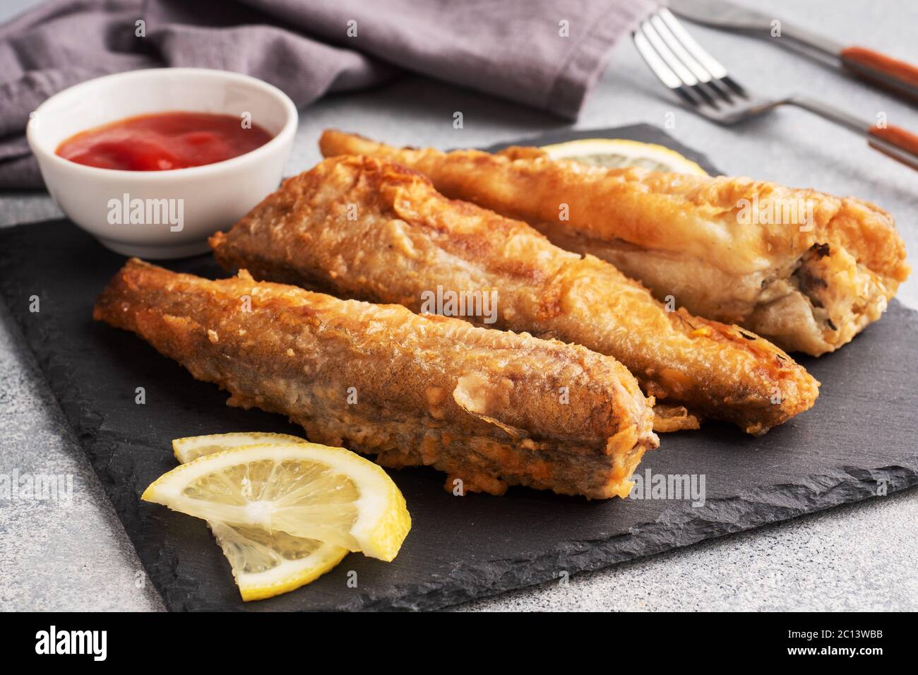 Fried fish hake Pollock with tomato sauce and slices of fresh lemon ...