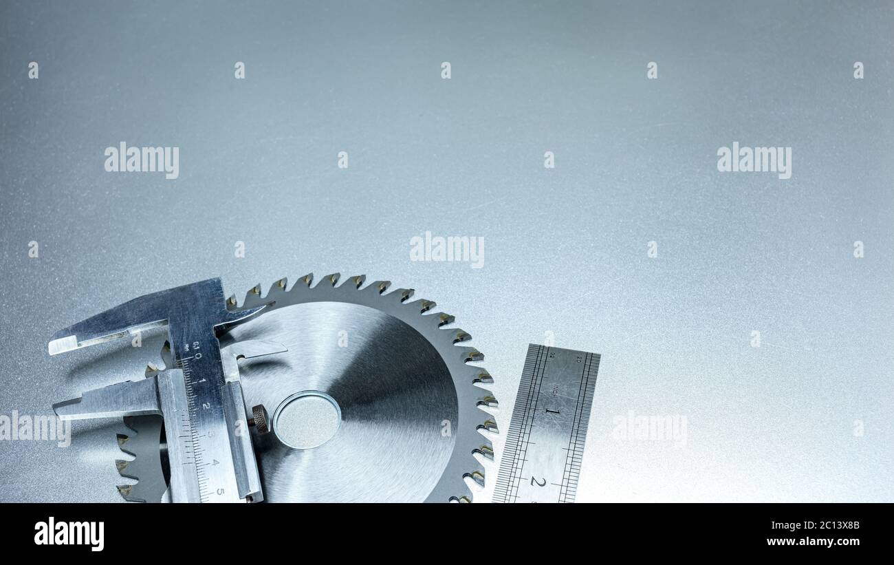 circular saw blade, standard rule and vernier caliper on grey metal ...