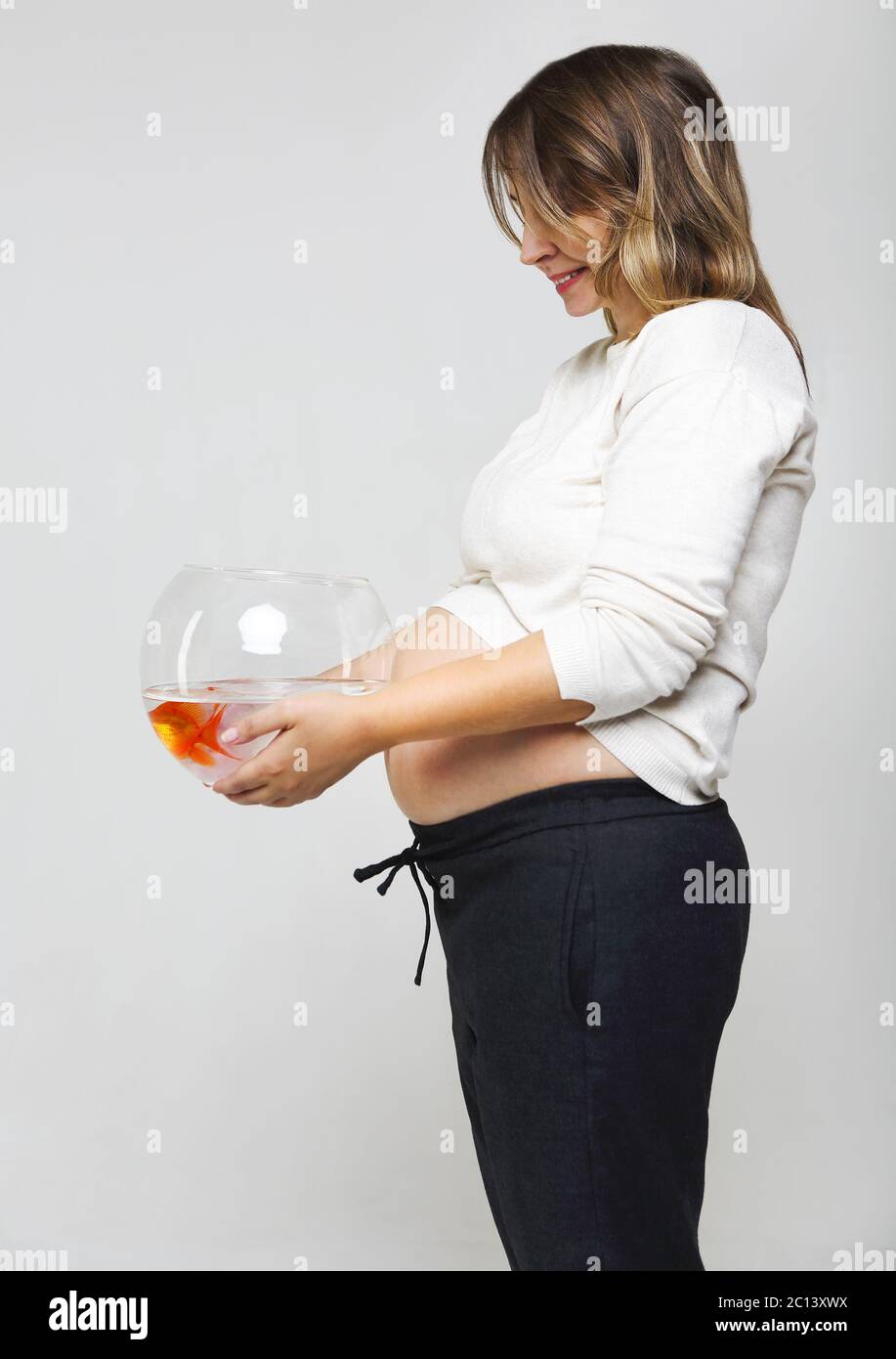 Happy pregnant woman holding a fishbowl with a goldfish in her hands ...