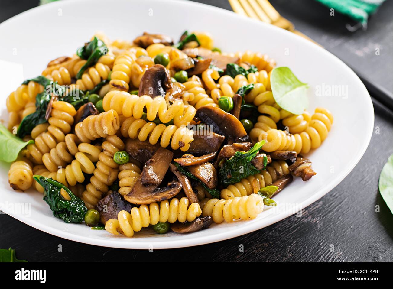Fusilli pasta with spinach and mushrooms on a white plate. Vegetarian ...