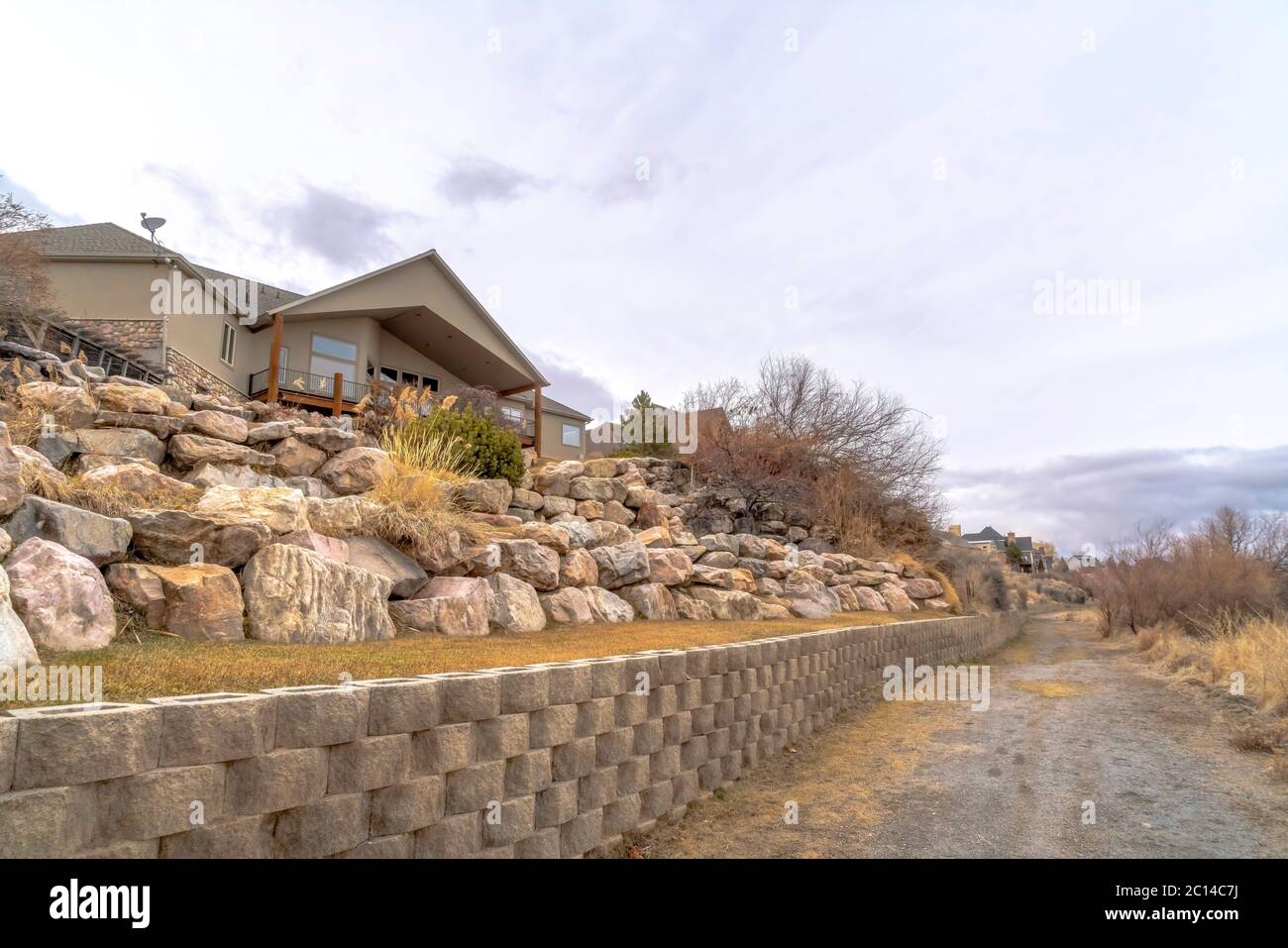 Dirt road along homes on a slope with huge rocks and concrete retaining ...