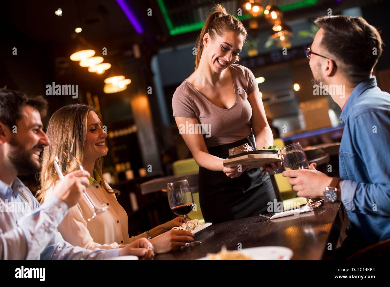 Pretty waiter woman serving group of friends with food in the restaura ...