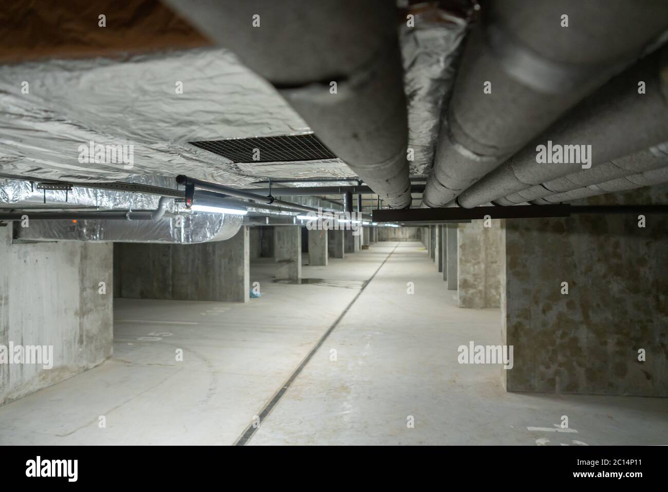 View along exposed ceiling pipes of an empty concrete basement in a ...