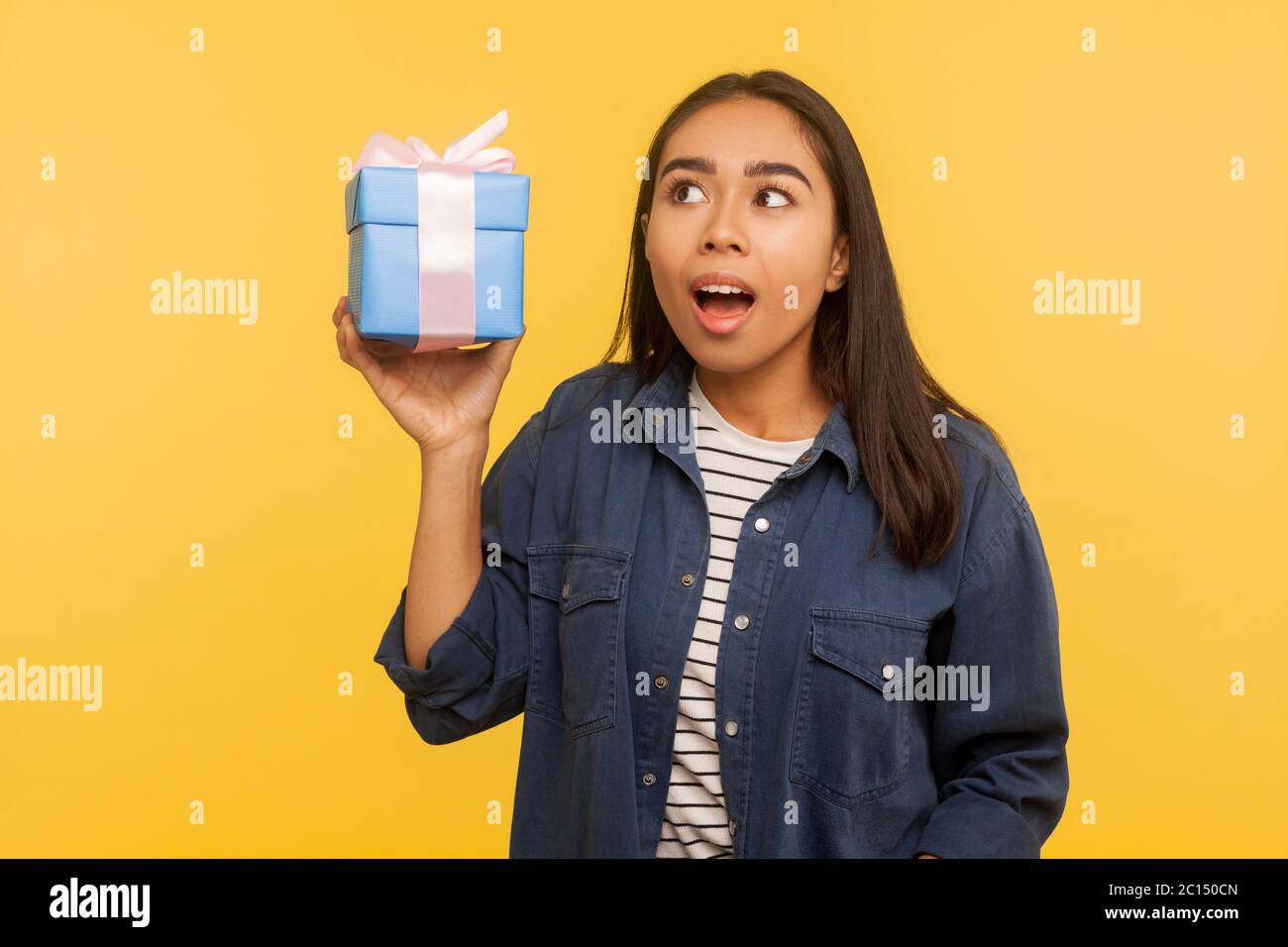 Portrait of funny amazed girl in denim shirt holding wrapped gift ...