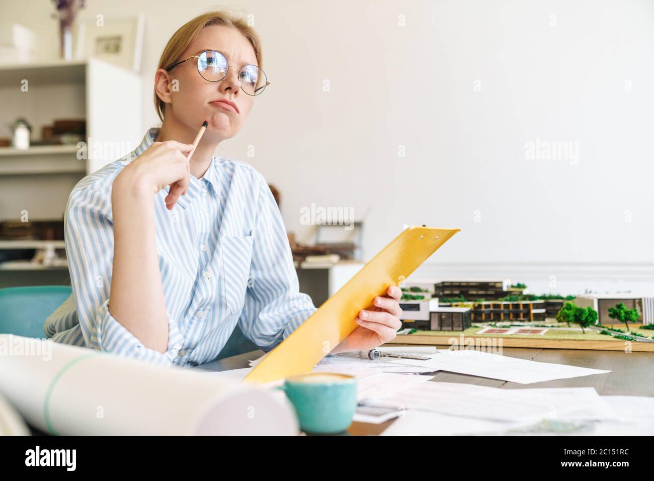 Photo of puzzled young woman architect in eyeglasses working with ...