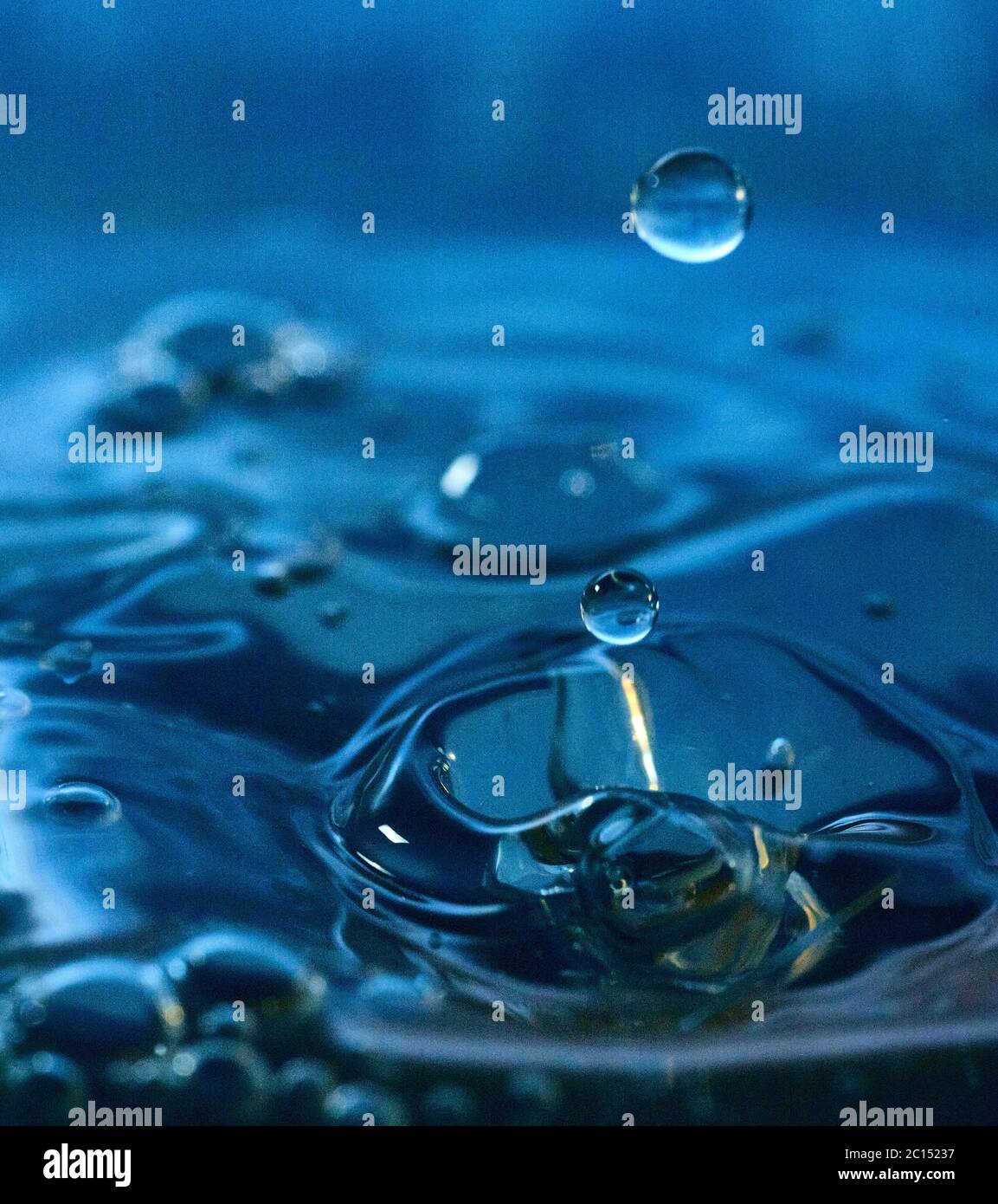 Water droplets falling on and bouncing off a pool of water, leaving ...