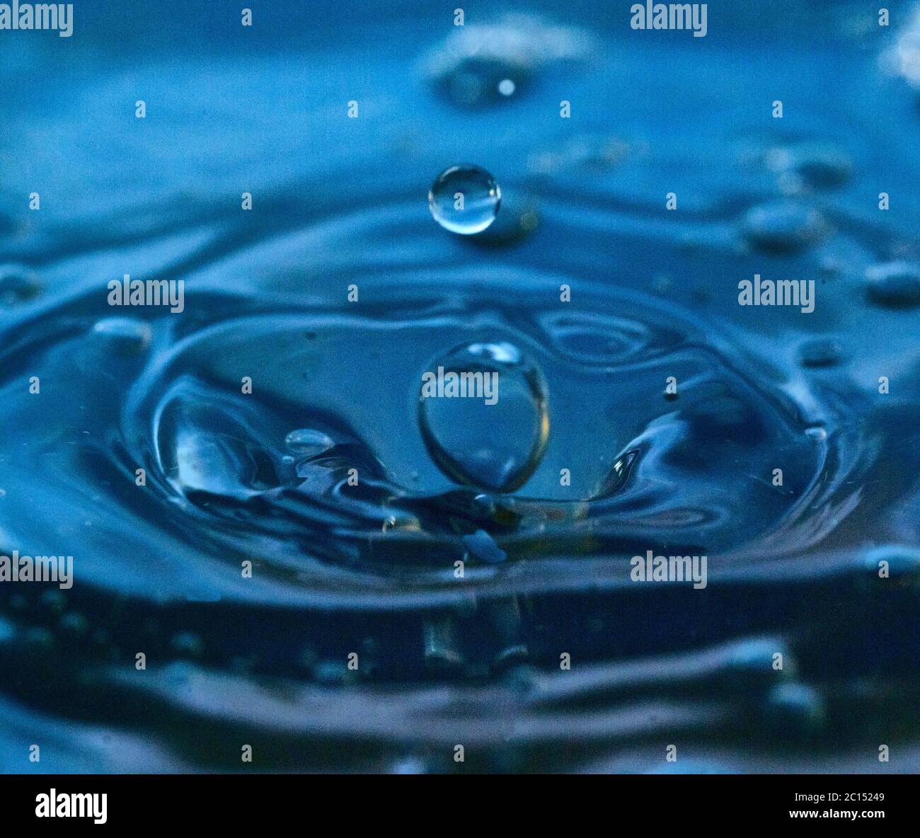 Water droplets falling on and bouncing off a pool of water, leaving ...
