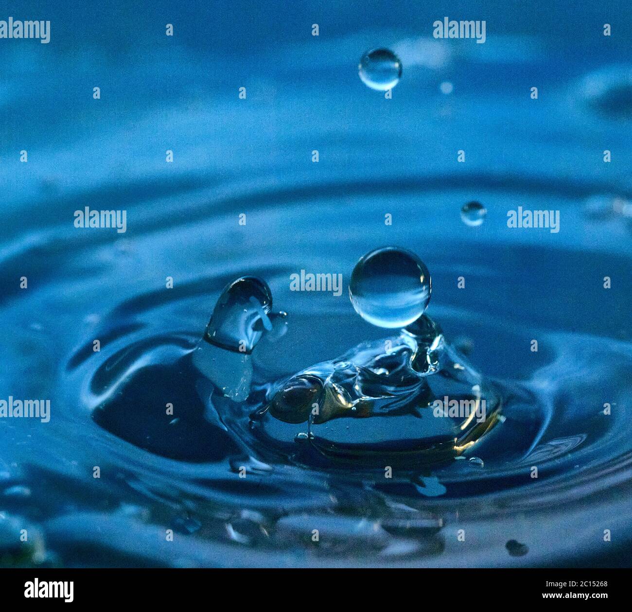 Water droplets falling on and bouncing off a pool of water, leaving ...