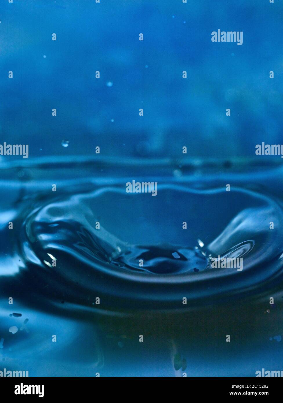 Water droplets falling on and bouncing off a pool of water, leaving ...