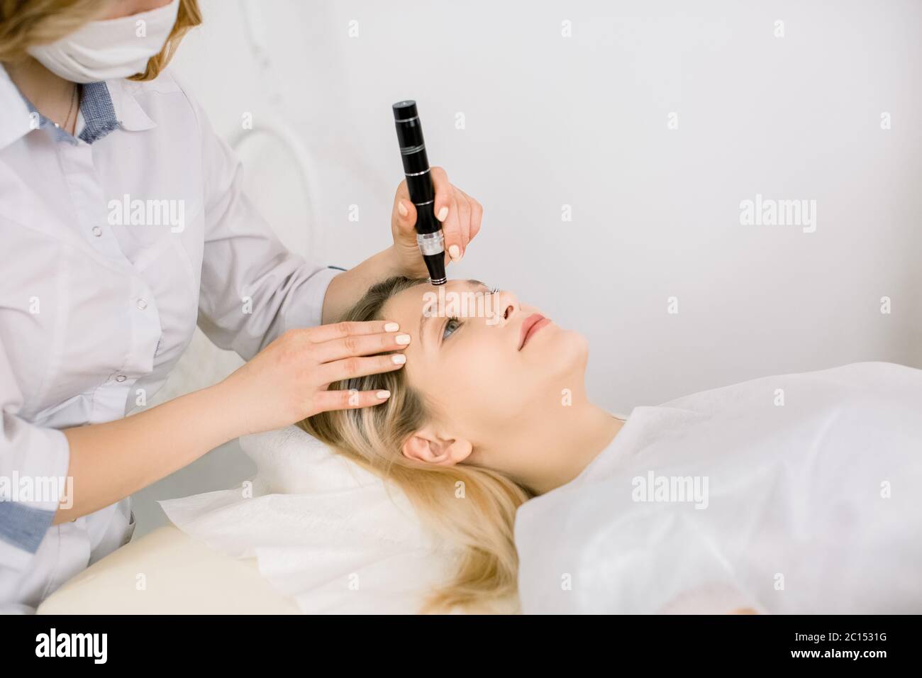 Young blond girl client lying on the couch in modern dermatology clinic ...
