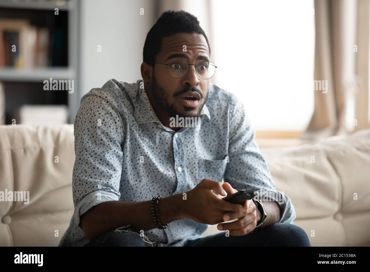 African guy holding remote control watching movie feels appalled Stock ...
