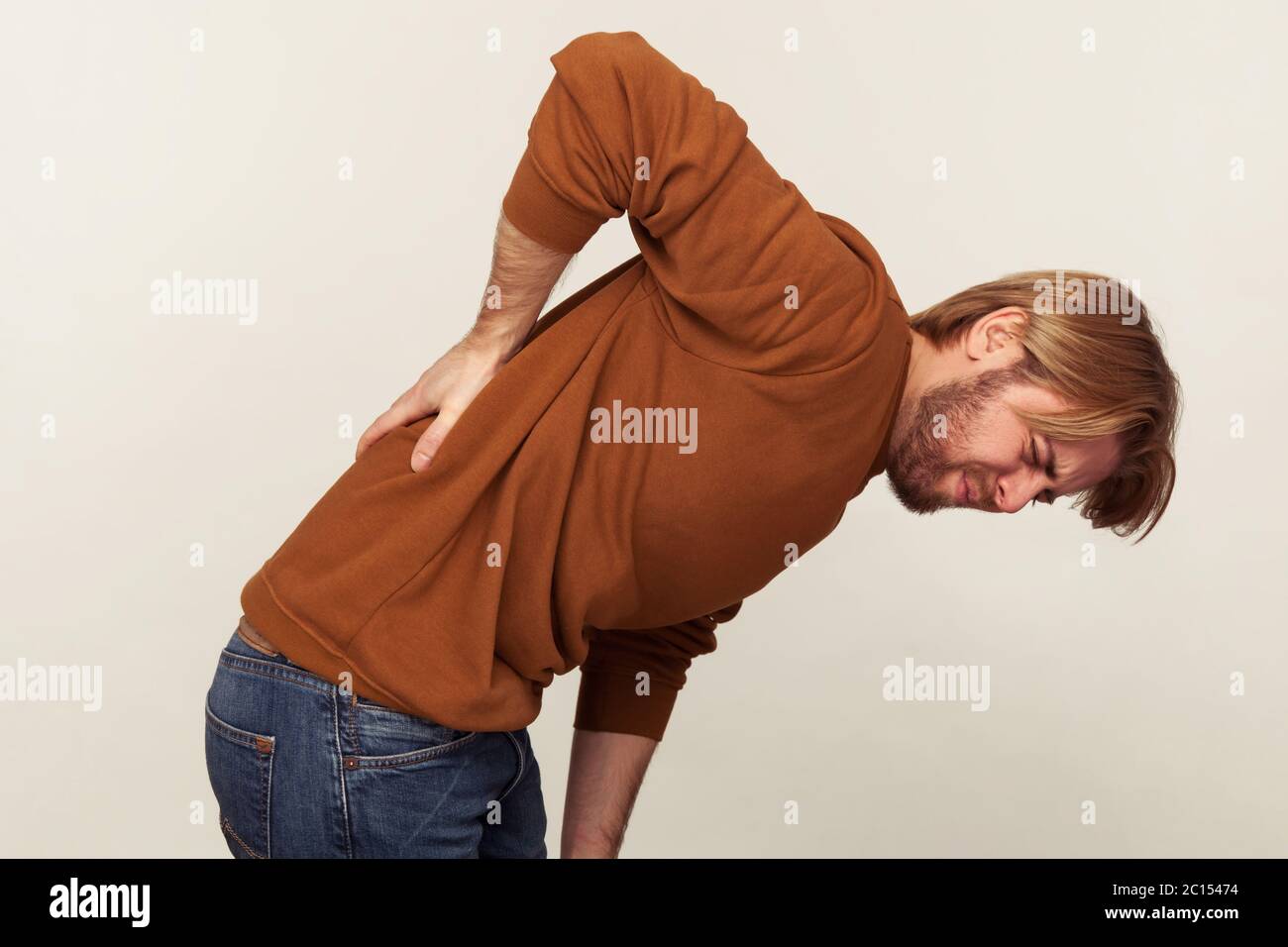 Side view of exhausted unhealthy young man hunching and touching aching ...