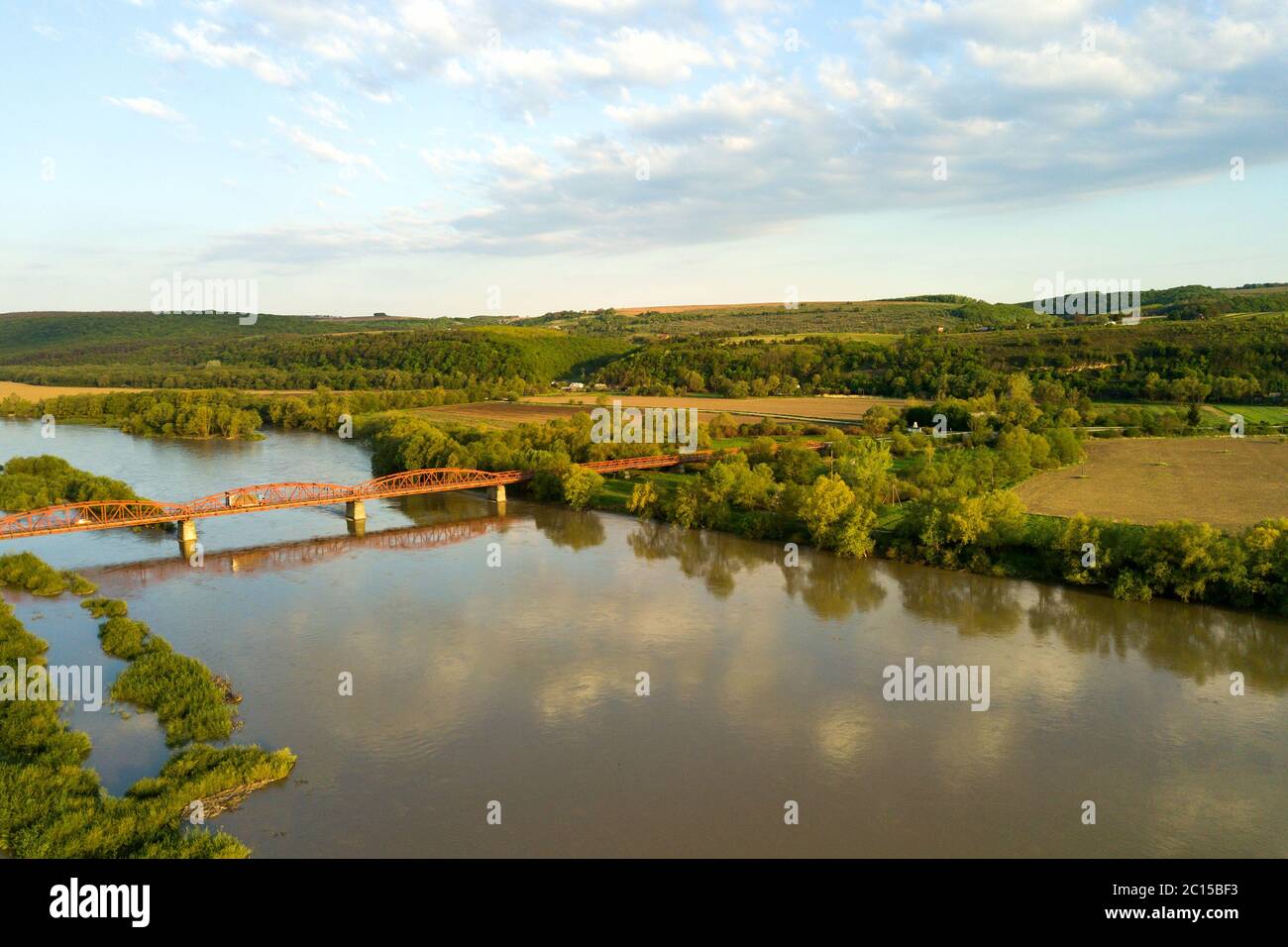Aerial view of a narrow road bridge stretching over muddy wide river in ...