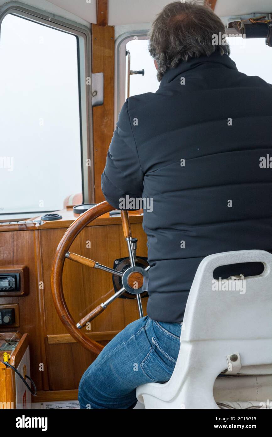Captain driving an old wooden boat - rear view Stock Photo - Alamy