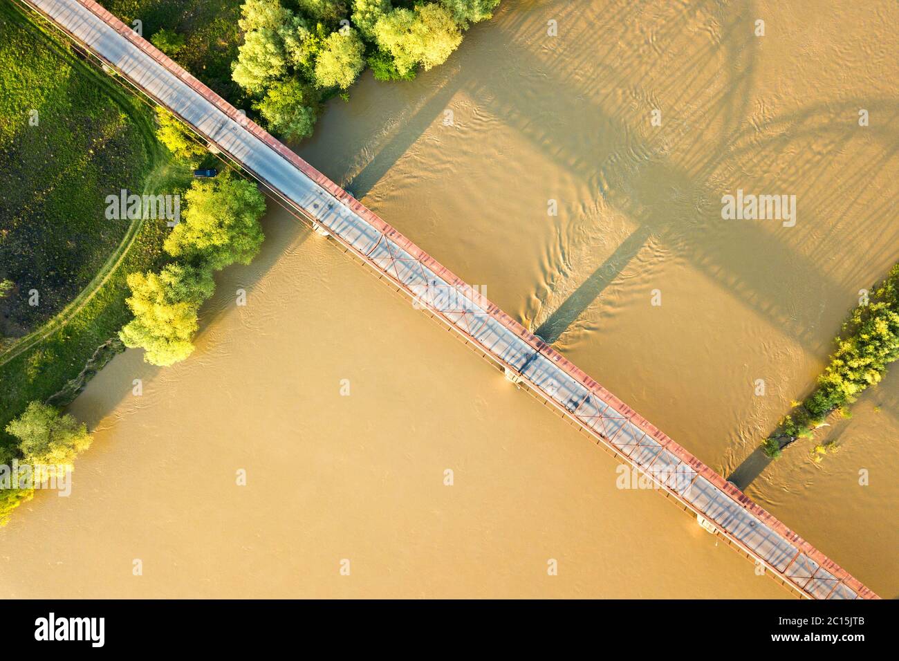 Aerial view of a narrow road bridge stretching over muddy wide river in ...