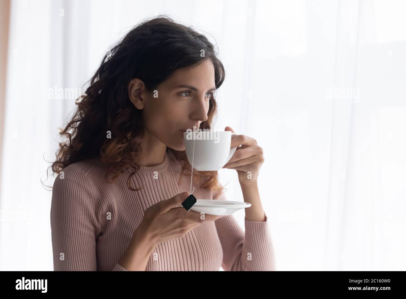Beautiful young woman drinking tea, looking at window Stock Photo - Alamy