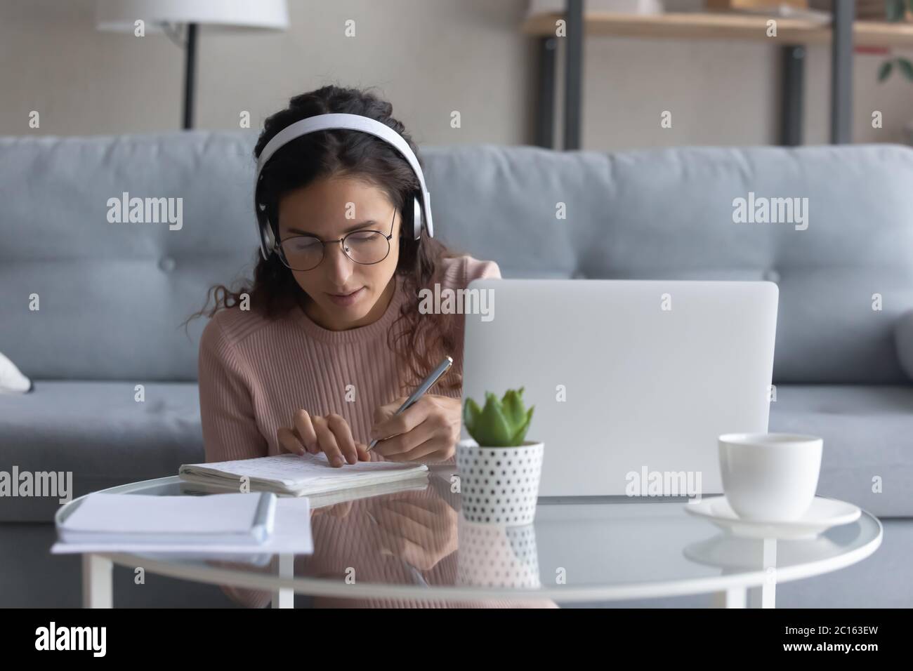 Focused woman wearing headphones doing school assignment, using laptop ...