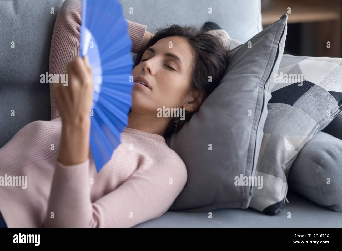 Exhausted overheated woman waving paper fan, lying on couch Stock Photo ...