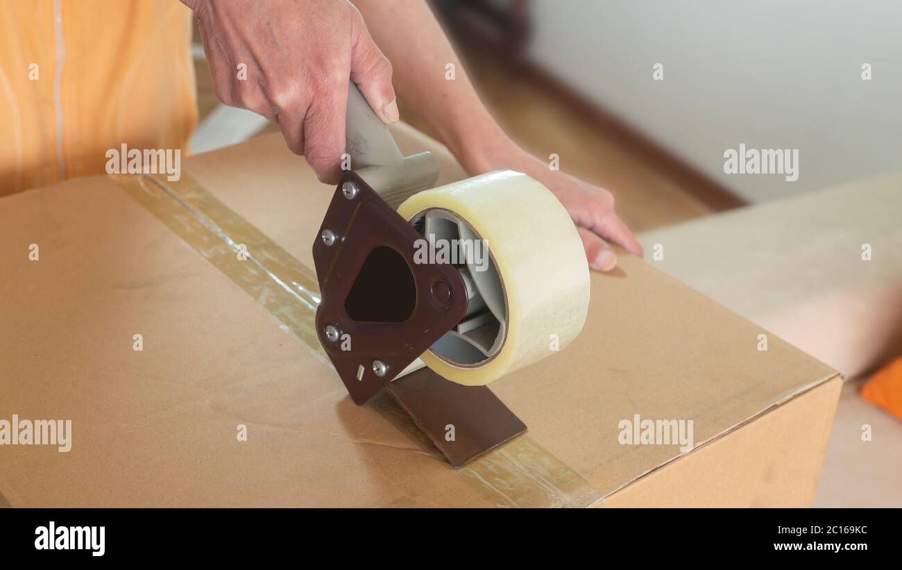 Close up on a woman's hands closing a cardboard box with adhesive tape ...