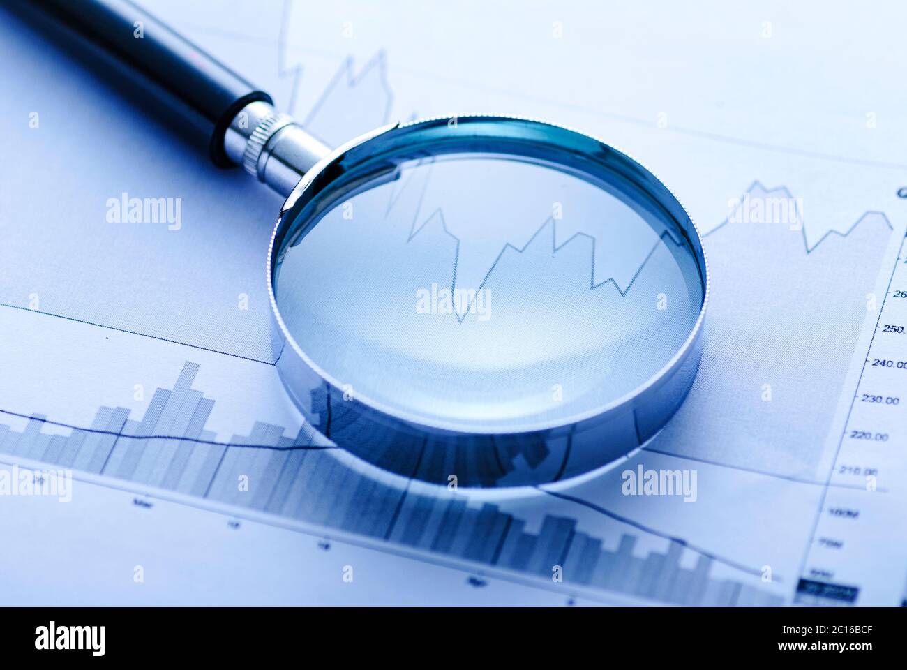 Magnifying glass with two fluctuating statistical business graphs in a ...