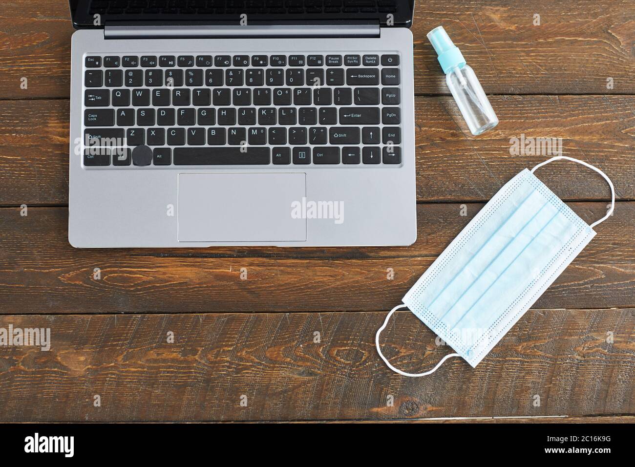 Top down view at laptop, face mask and hand sanitizer over dark wooden ...