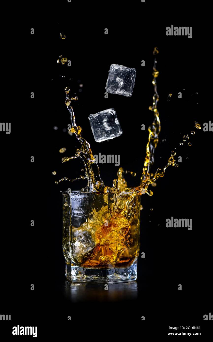 Glass of splashing whiskey or other alcohol with ice cube isolated on ...