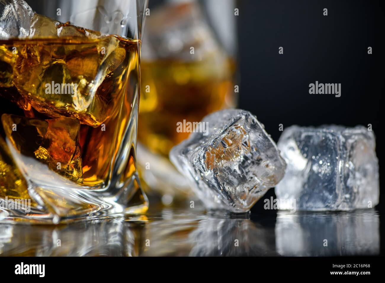 Glass of whiskey or other alcohol with cube ice on black background ...
