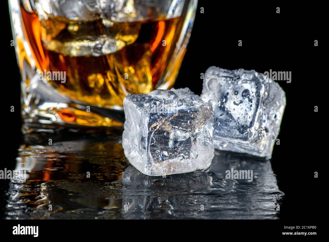 Glass of whiskey or other alcohol with cube ice on black background ...