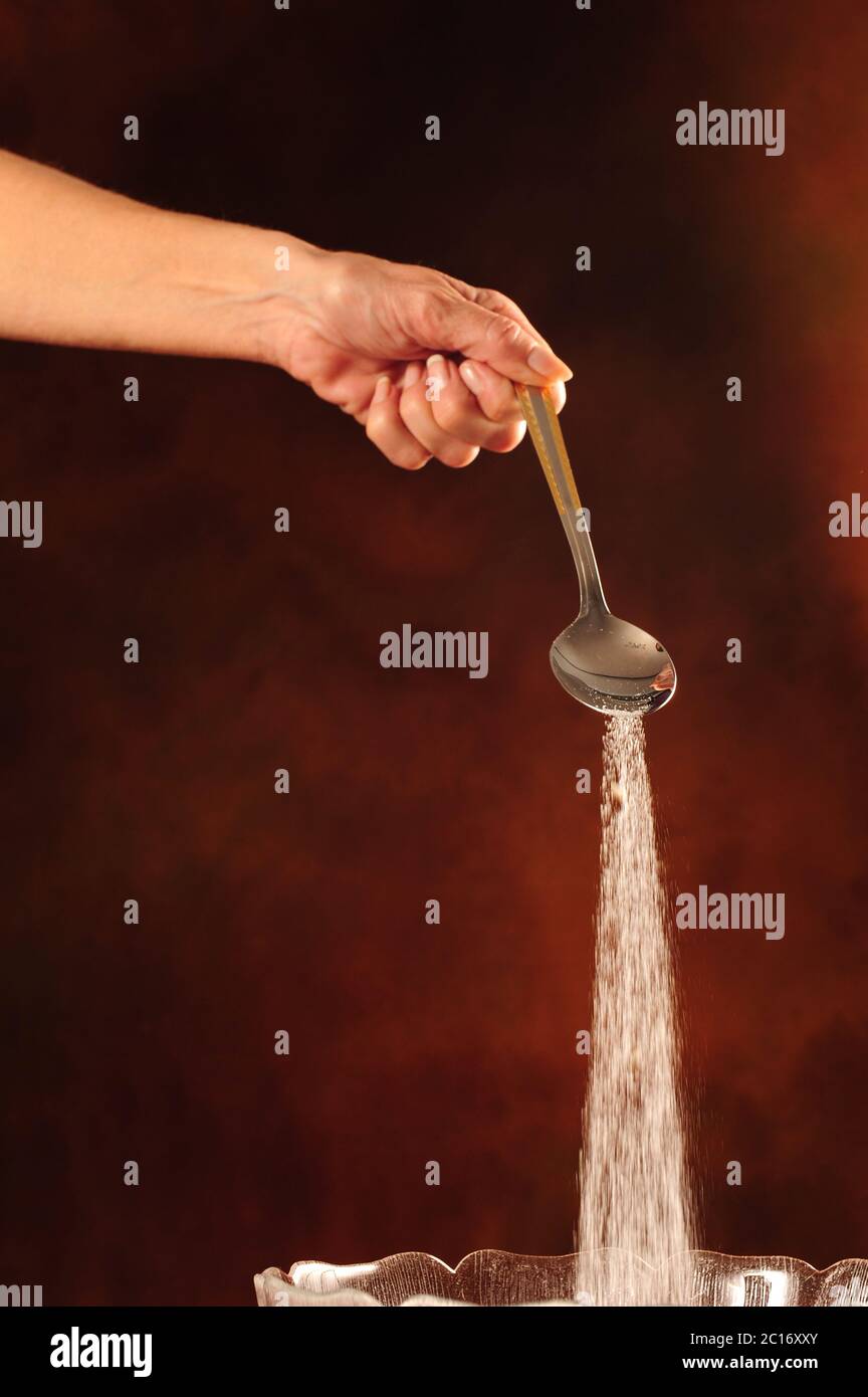 Woman's hand holding spoon of sugar. White sugar running off spoon ...