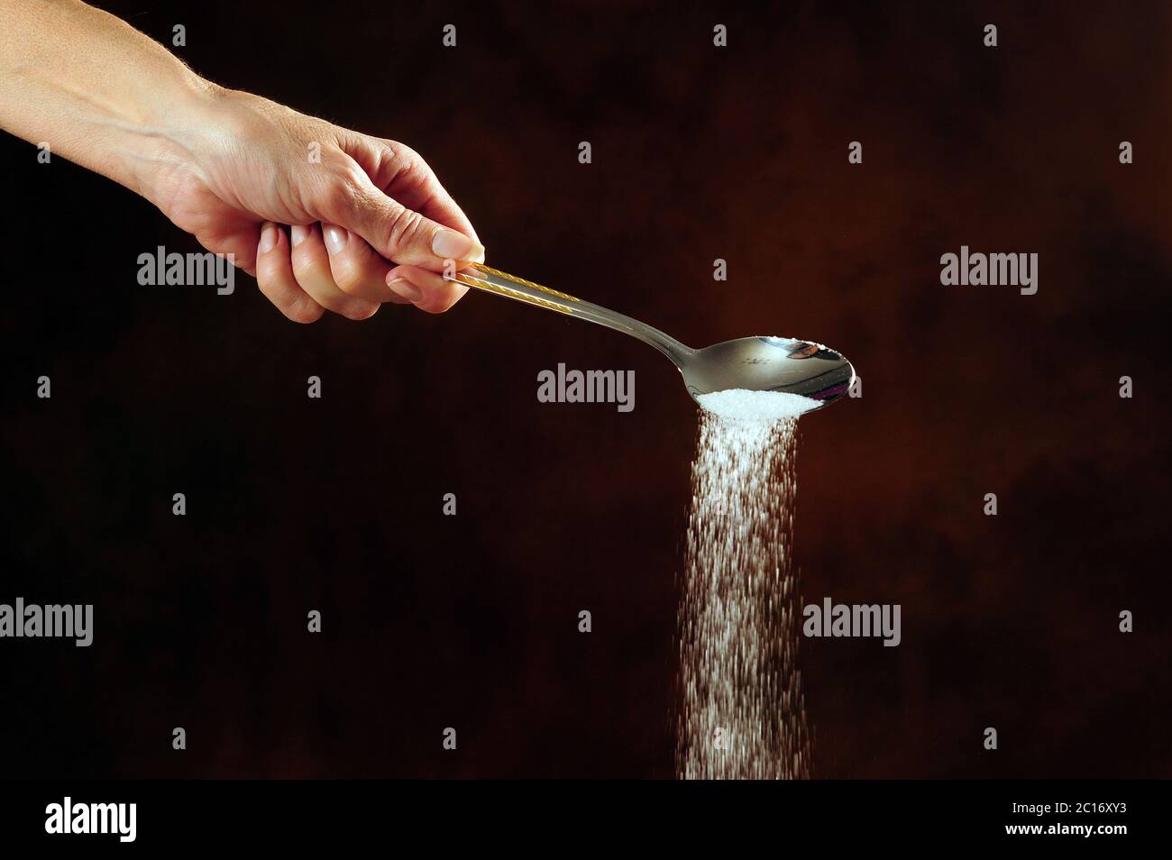 Woman's hand holding spoon of sugar. White sugar running off spoon ...