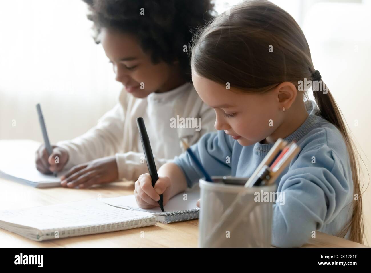 African and Caucasian schoolgirl mates sit at table writing task Stock ...