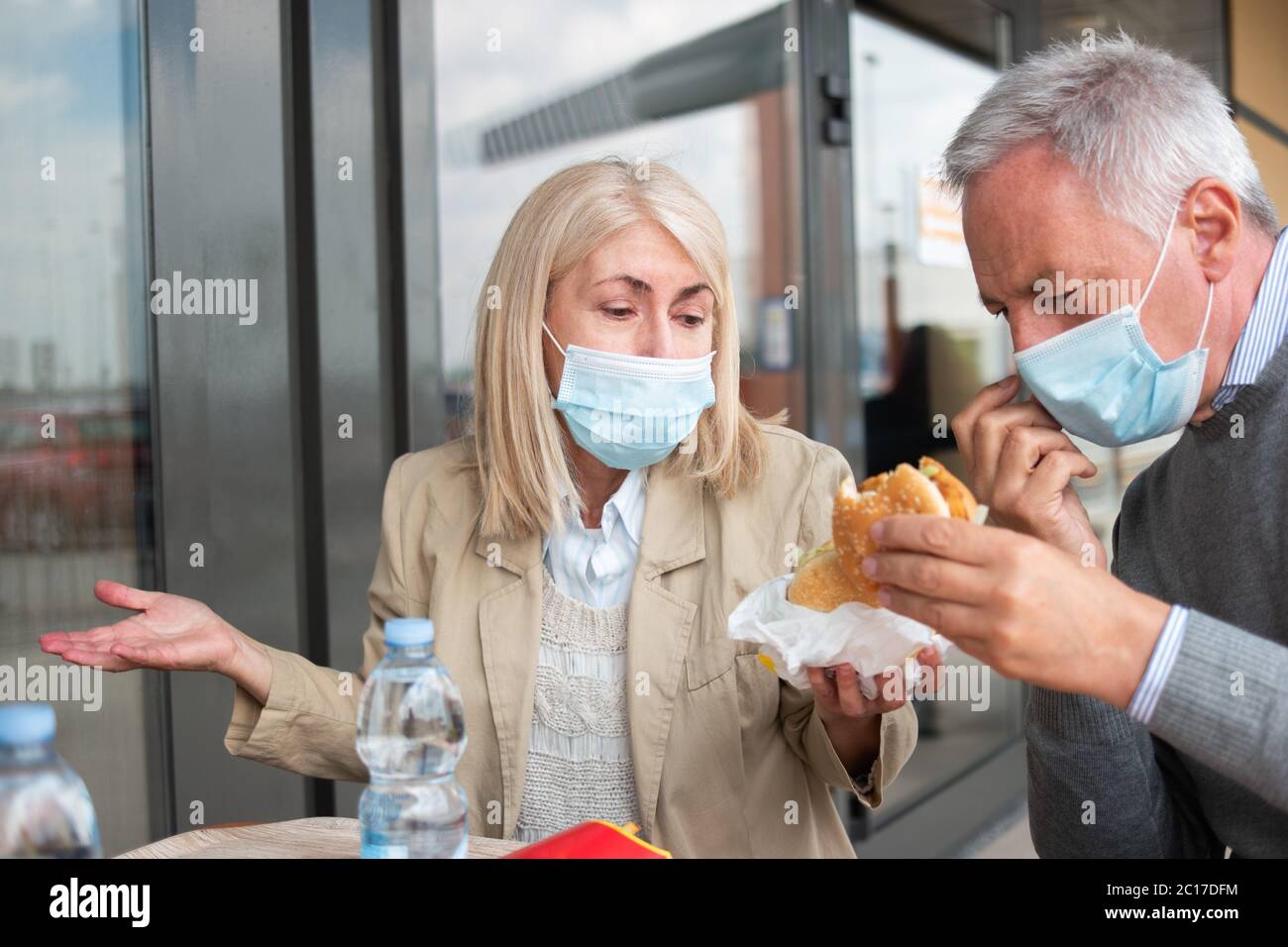 Senior couple trying to eat their fast food lunch hamburger while ...