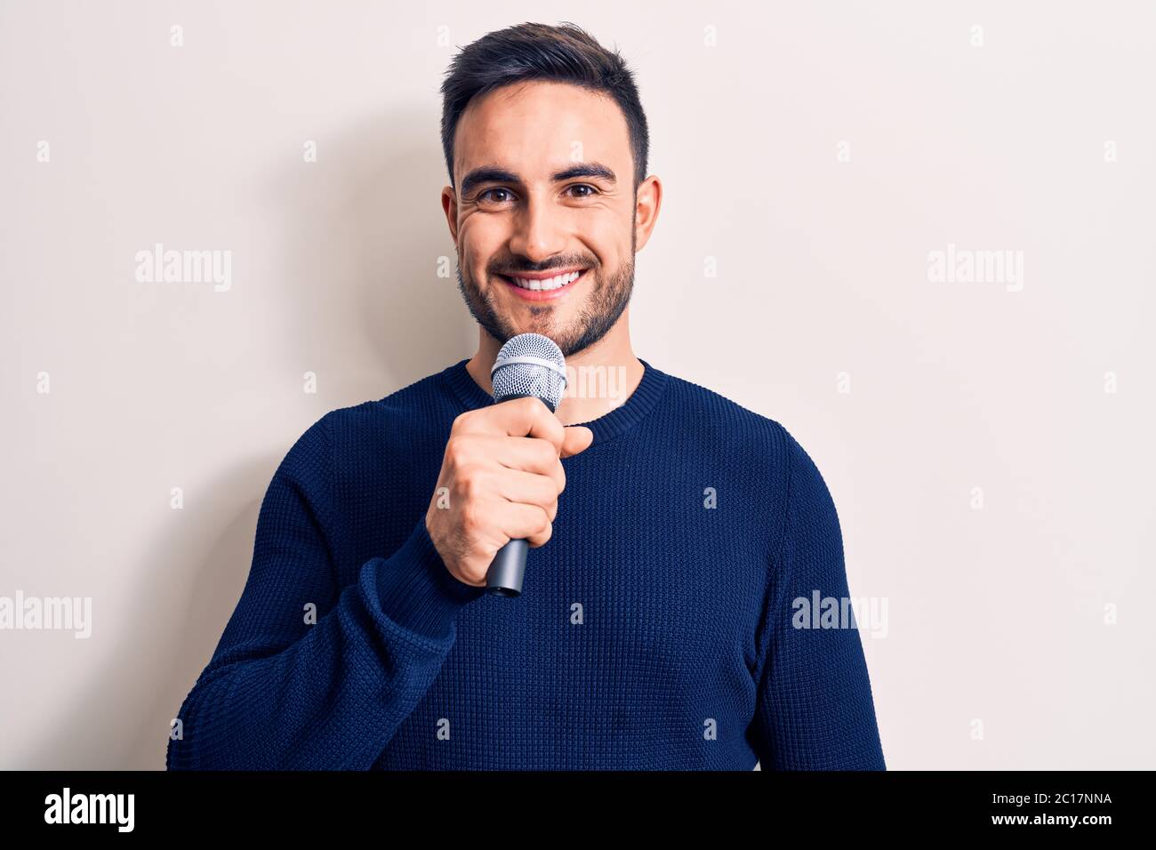 Young handsome singer man with beard singing song using microphone over white background looking ...